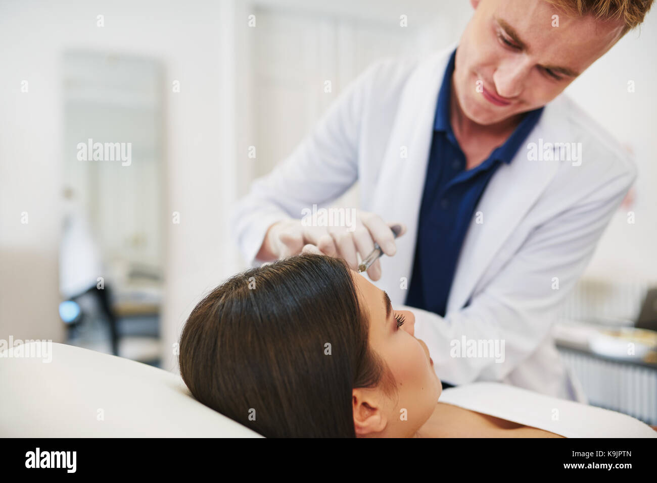 Young male doctor performing a botox injection to the forehead of a ...