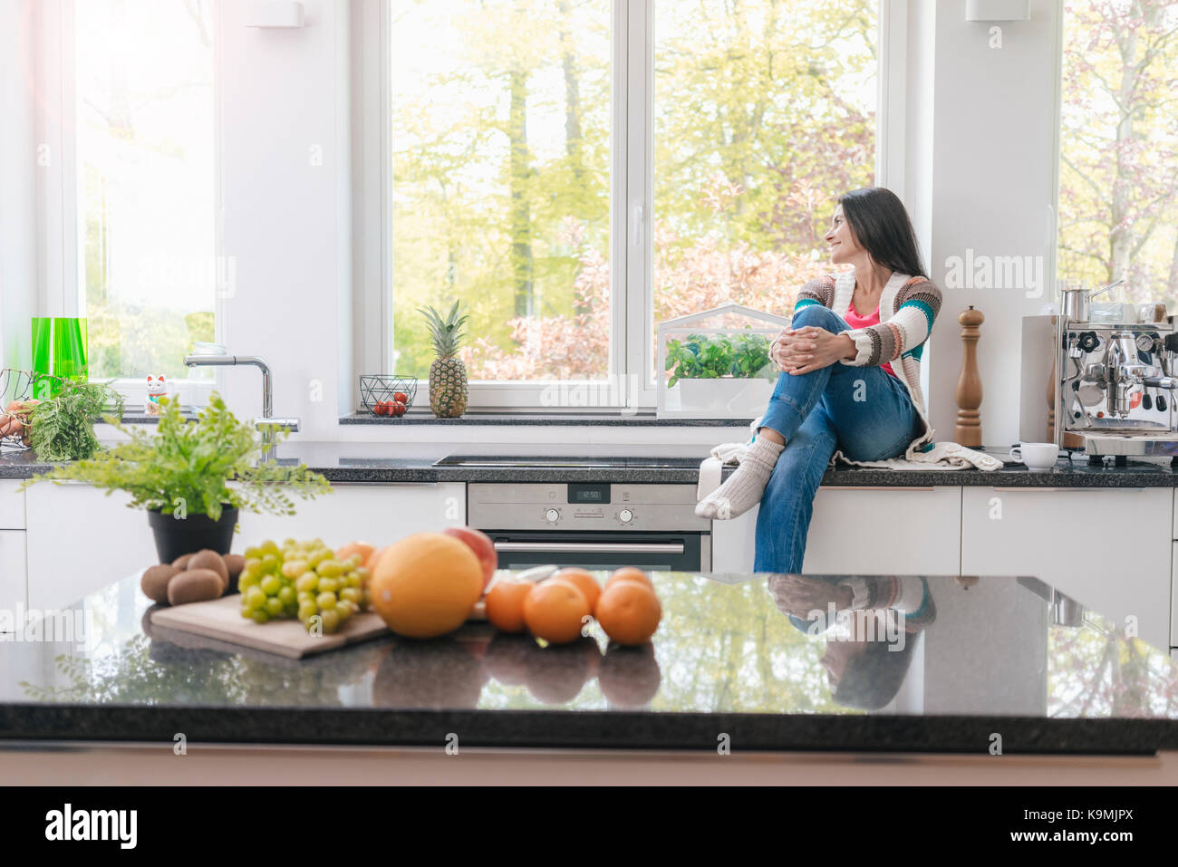 Smiling woman in kitchen looking out of window Stock Photo - Alamy