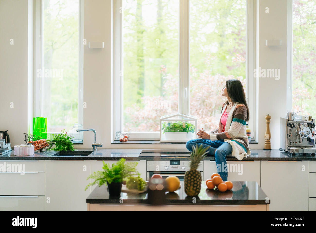 Woman in kitchen looking out of window Stock Photo - Alamy