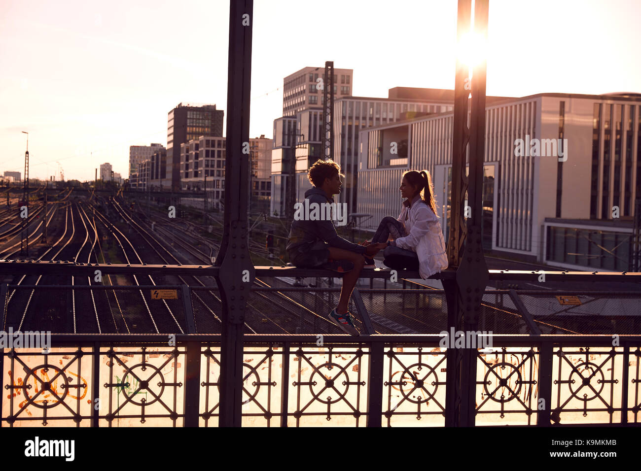 Germany, Munich, Young couple sitting on bridge, enjoying sunset Stock ...