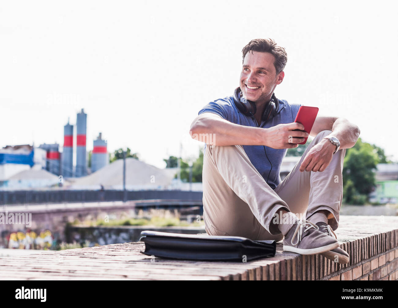 Businessman sitting on a wall, using smartphone Stock Photo - Alamy