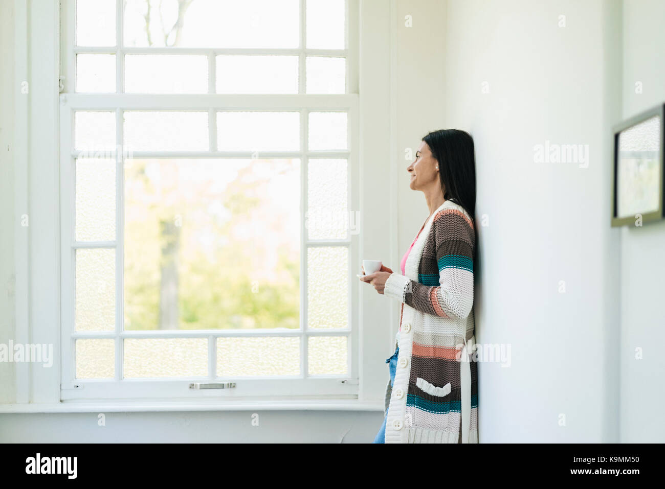 Woman at home looking out of window Stock Photo - Alamy