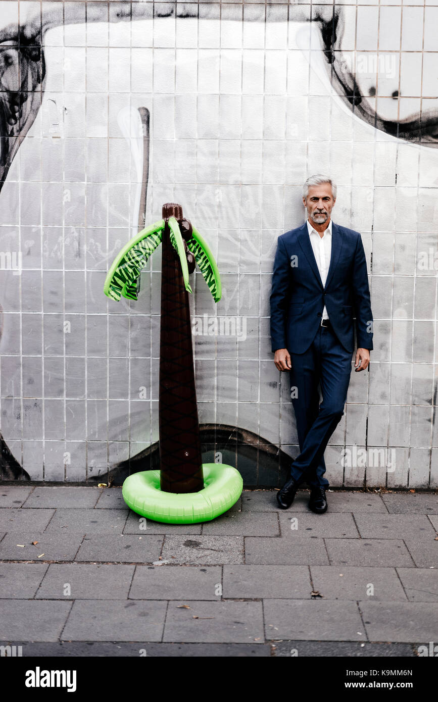 Mature businessman outdoors with inflatable palm tree Stock Photo - Alamy