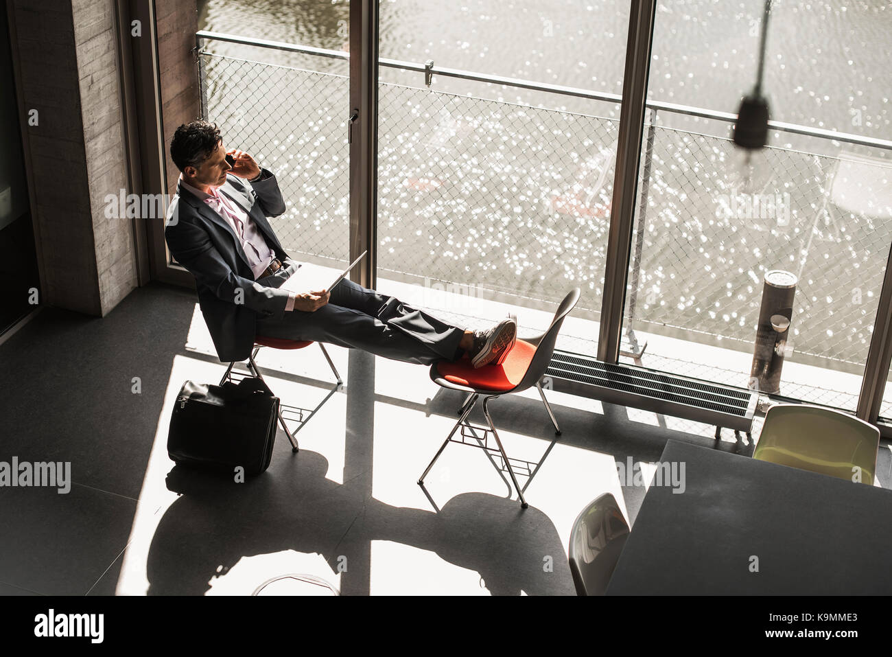 Businessman sitting at the window with feet up, working on laptop and ...