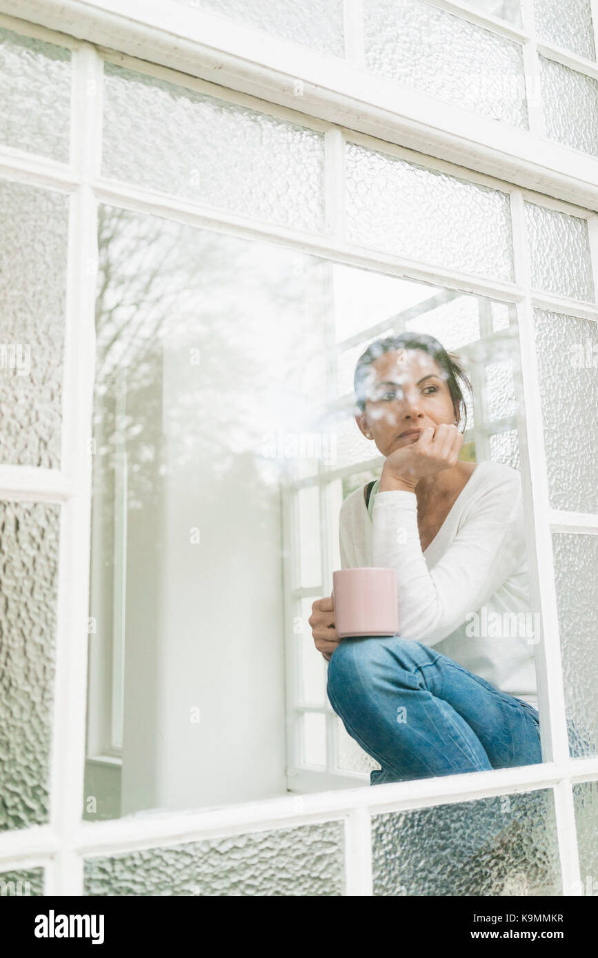 Pensive woman with cup of coffee looking out of window Stock Photo - Alamy