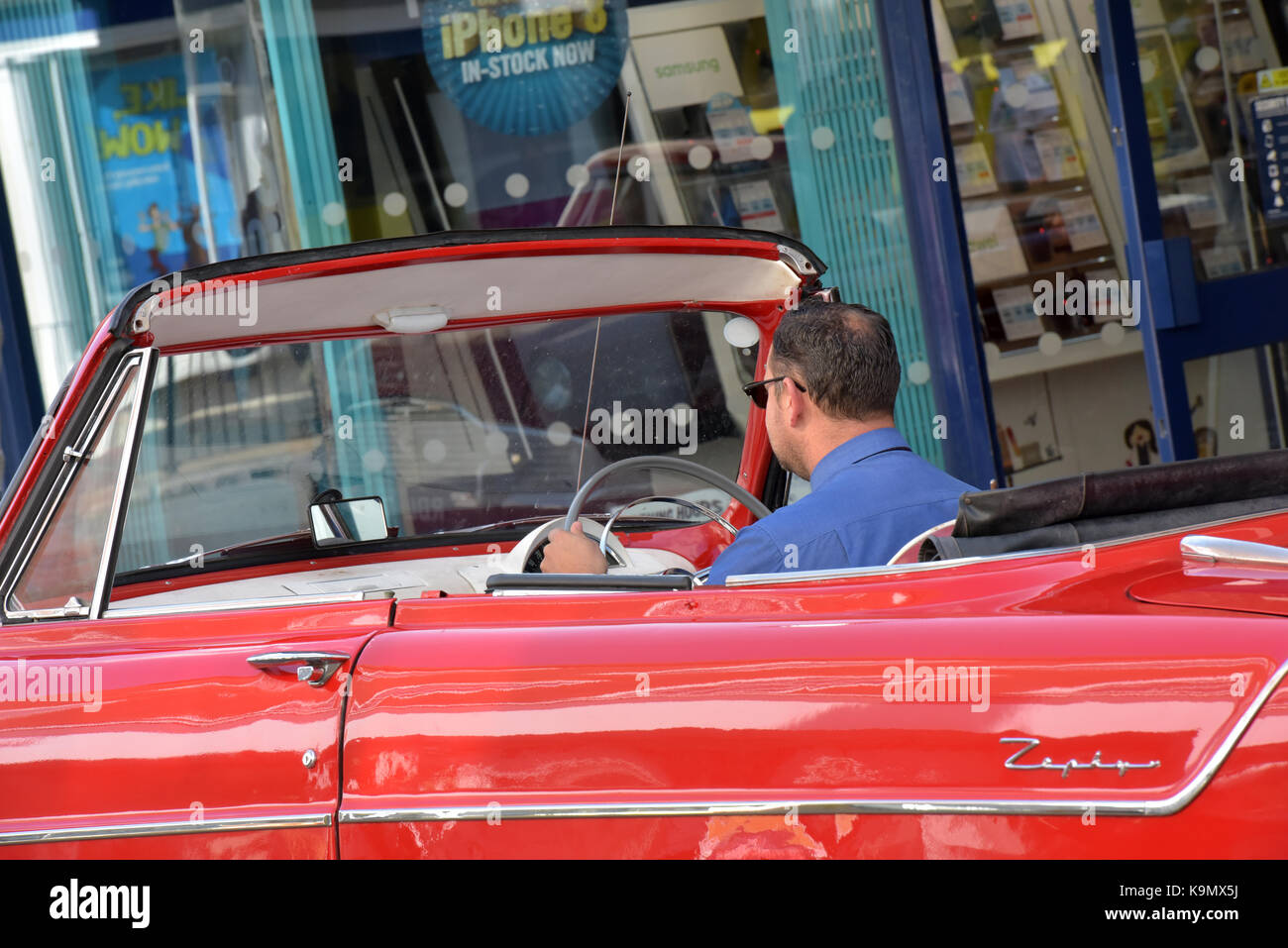 A man driving a red coloured classic convertible car along a town ...