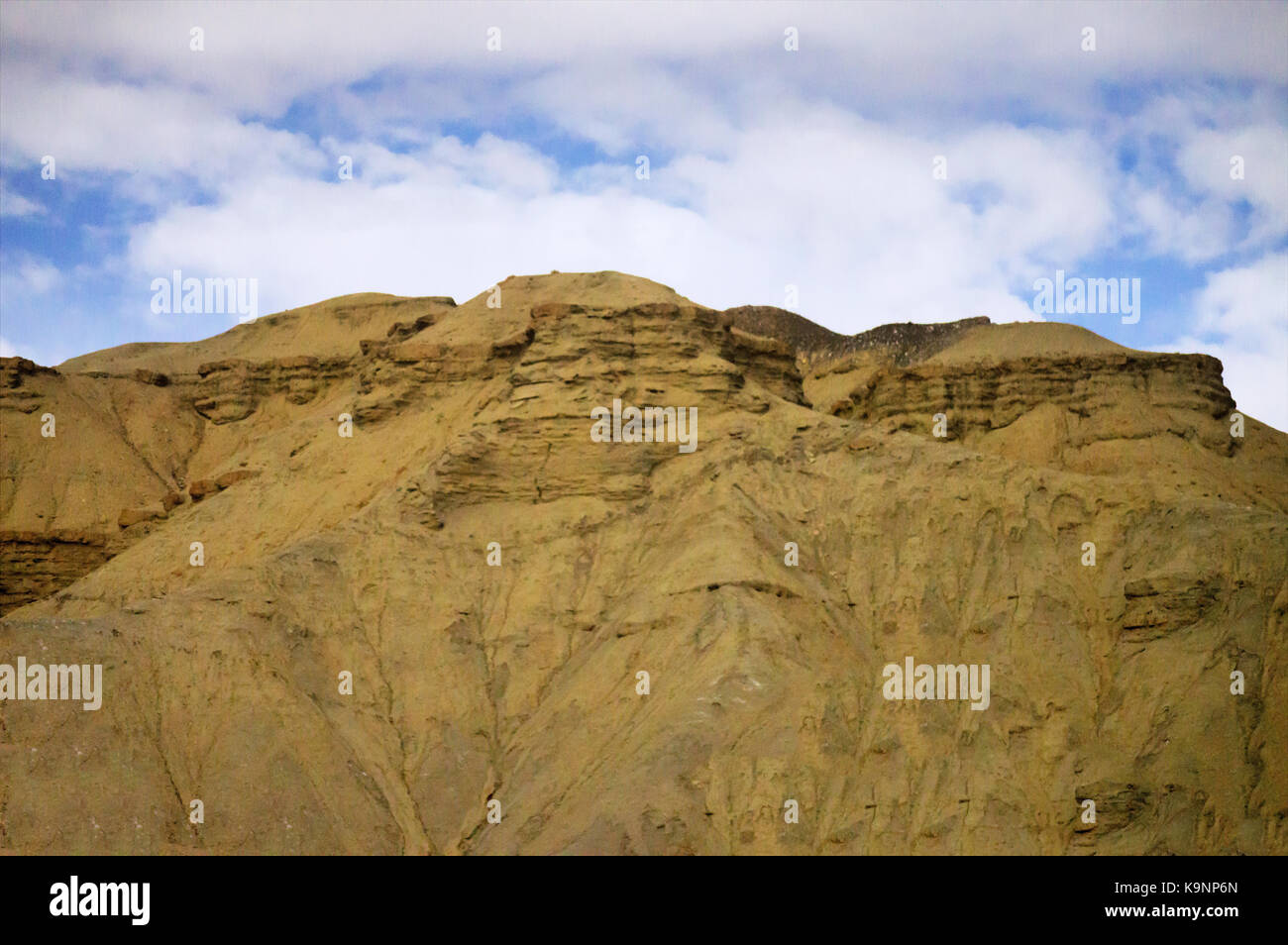 A beautiful natural tan rock wall on a blue sky with floating, puffy ...