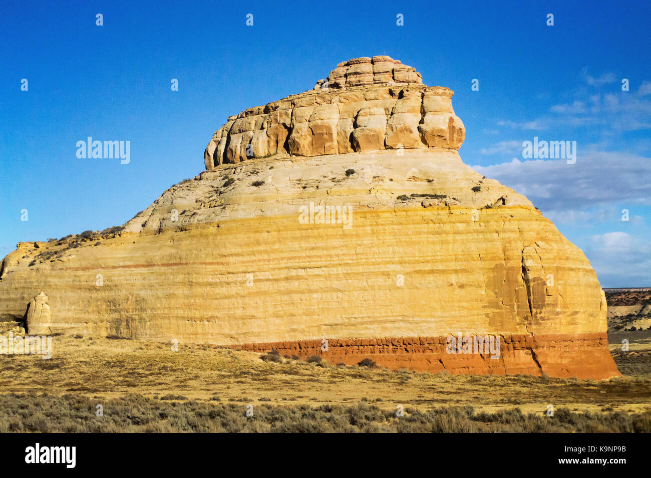 A huge vertical yellow layered sandstone formation on a clear blue sky ...
