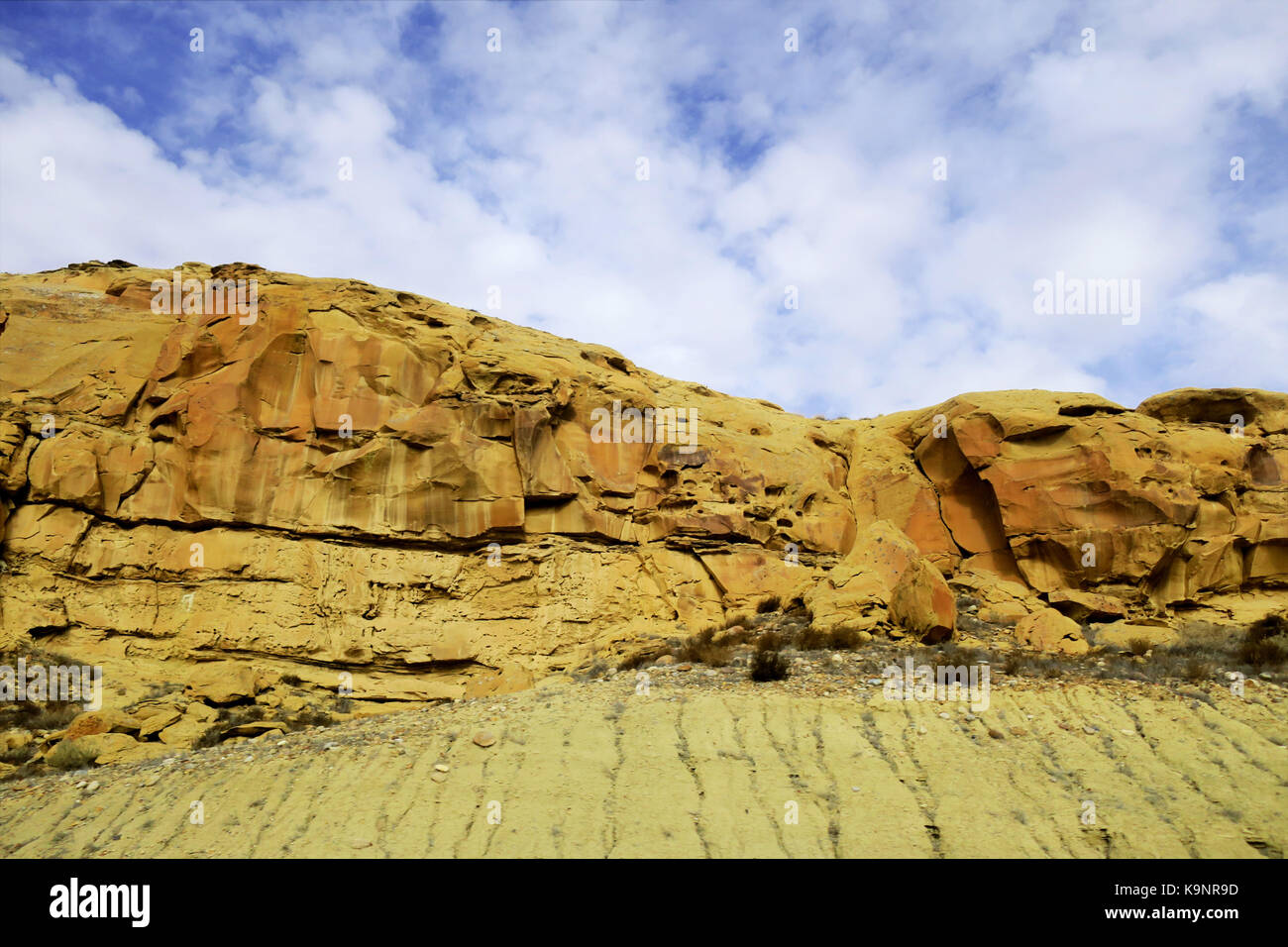 A beautiful natural tan rock wall on a blue sky with floating, puffy ...