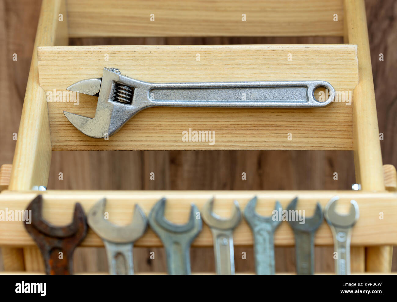 Old adjustable wrench lies on the step of a wooden ladder against the ...