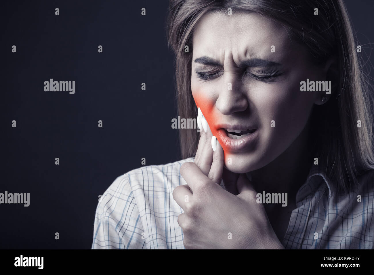 Young woman is suffering from a toothache against a dark background ...