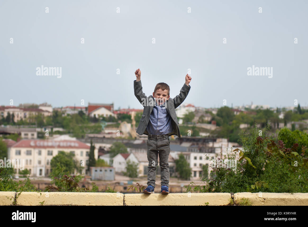 shouting little boy in a jacket raised both hand up on sea port ...