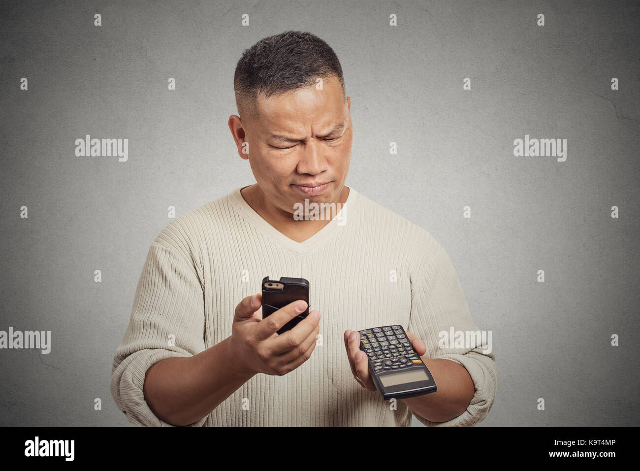 Confused man looking at his smart phone holding calculator isolated on ...