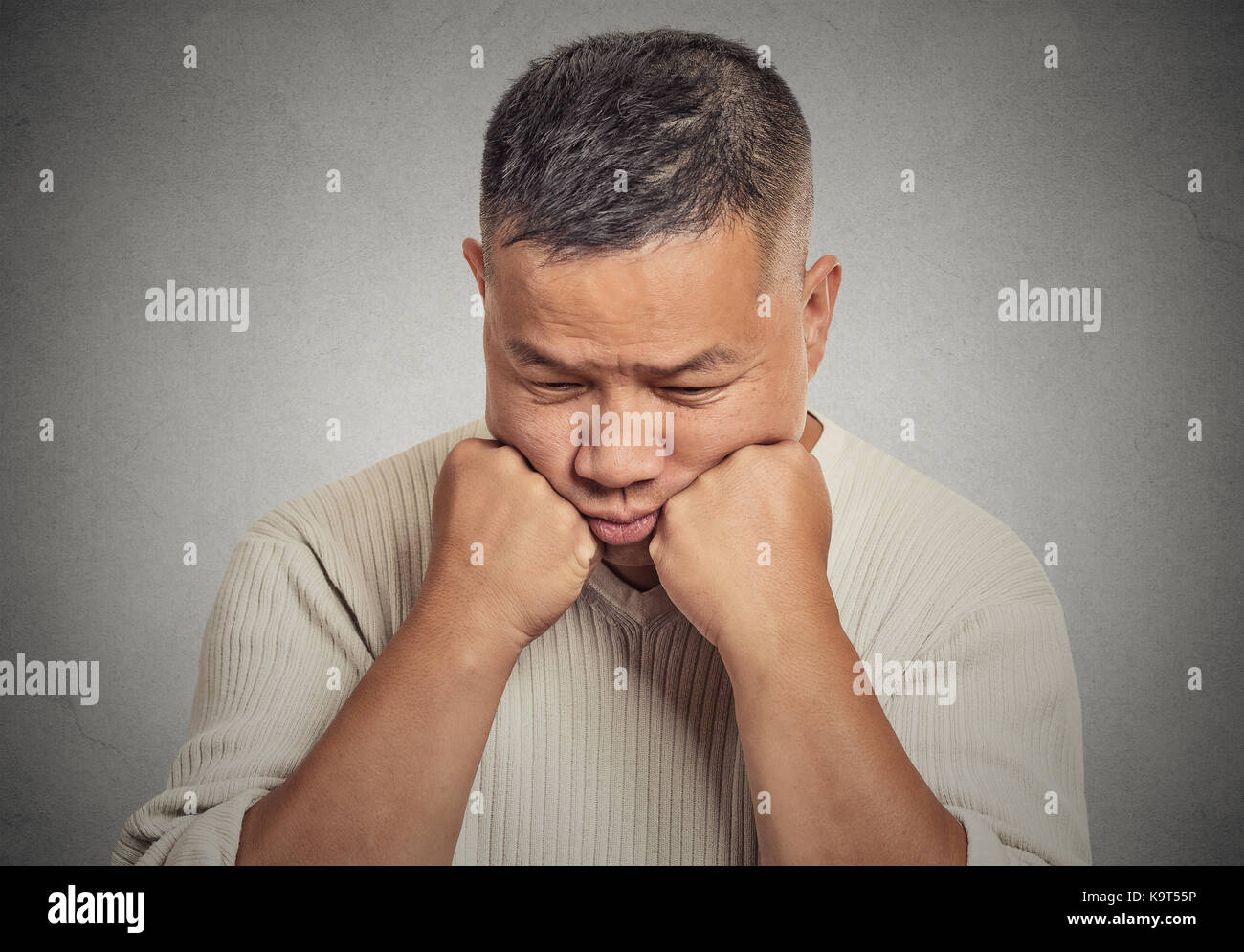 Headshot portrait of a sad young man looking down isolated on grey wall ...