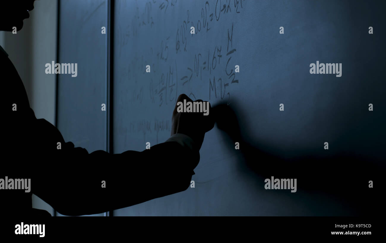 Scientist writing formulas on chalkboard. Hand with chalk wrote physics ...