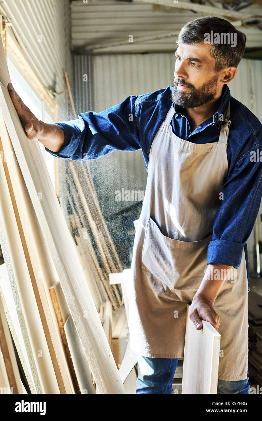 Portrait of skilled carpenter gently touching smooth piece of wood in ...