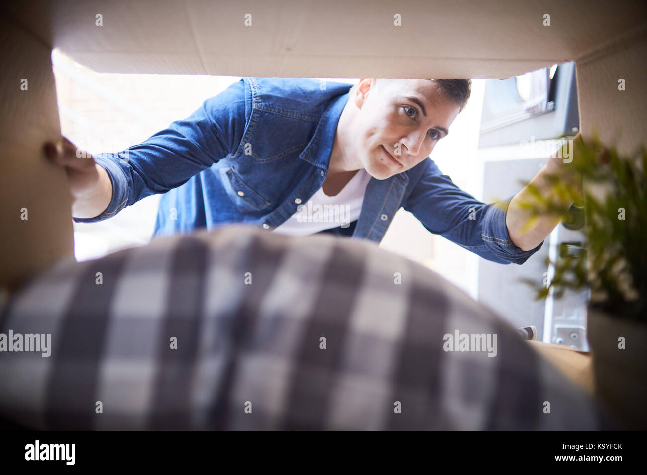 Portrait of smiling young man looking into box to check if he is ready ...