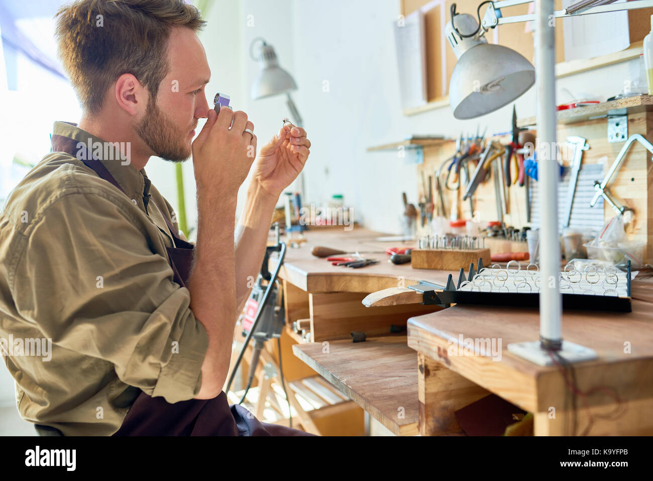 Side view portrait of jeweler looking at ring through magnifying glass ...