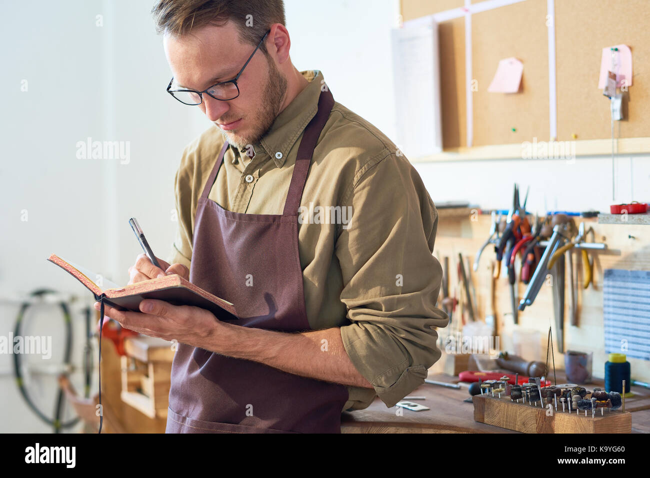 Portrait of young craftsman drawing sketches holding open book while ...
