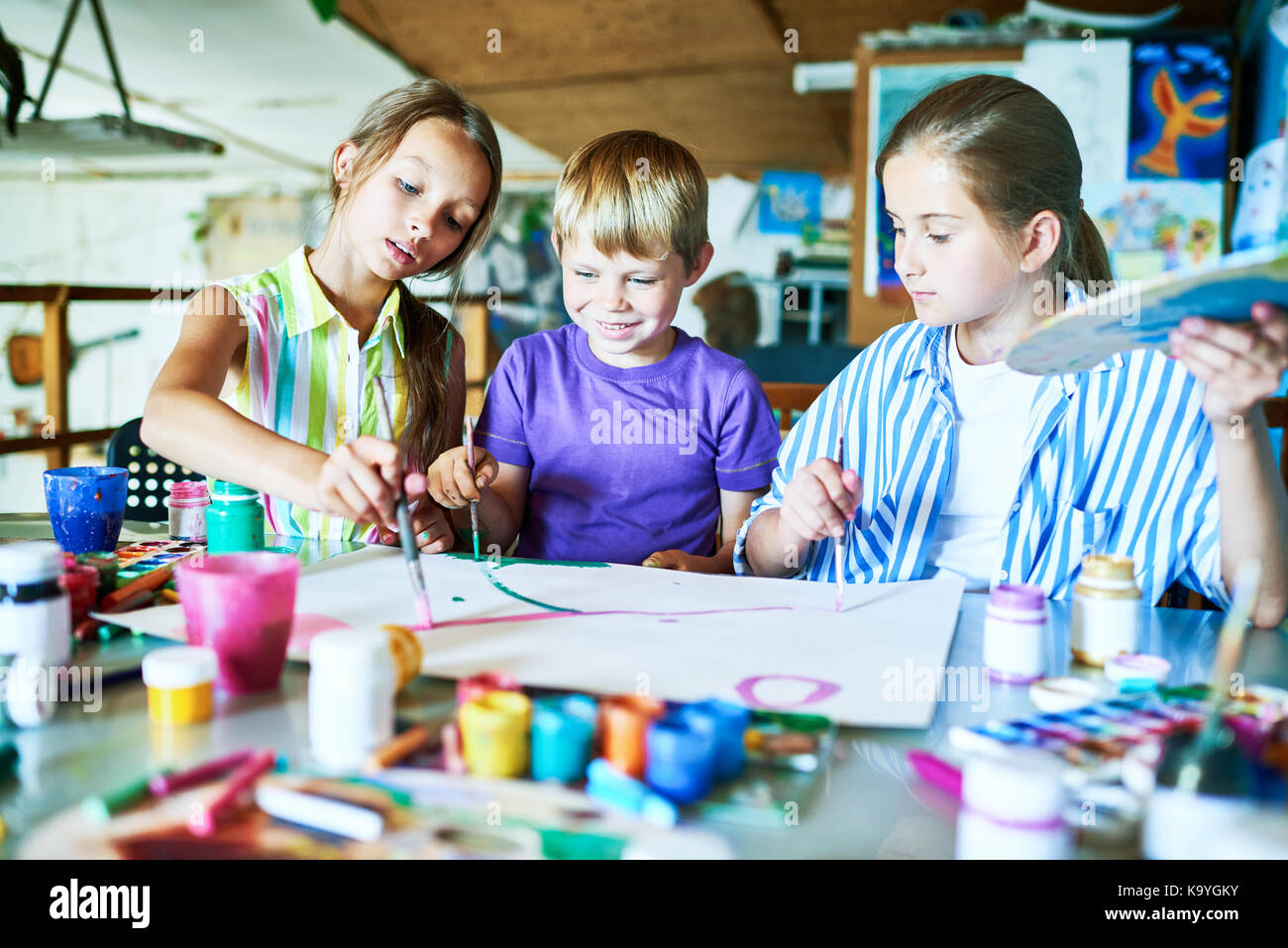 Portrait of three children painting picture together smiling happily ...