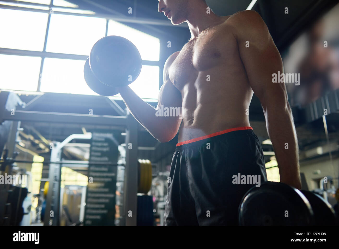 Low angle view of young bodybuilder with bare muscular torso doing ...