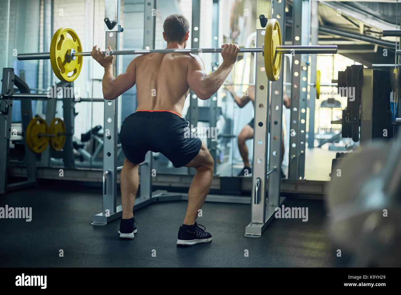 Back view of young bodybuilder flexing muscles with barbell in front of ...