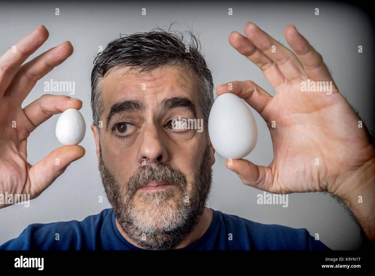 Man compares ironically two eggs one of smaller size, isolated on white ...