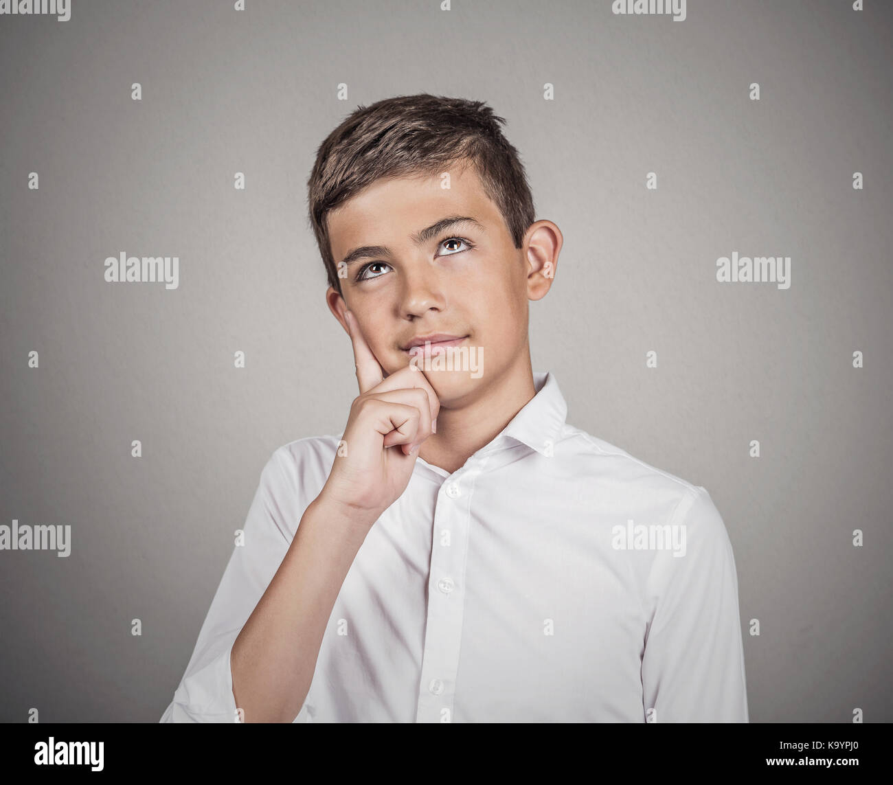 Portrait thinking, daydreaming teenager boy, finger on face, looking up ...