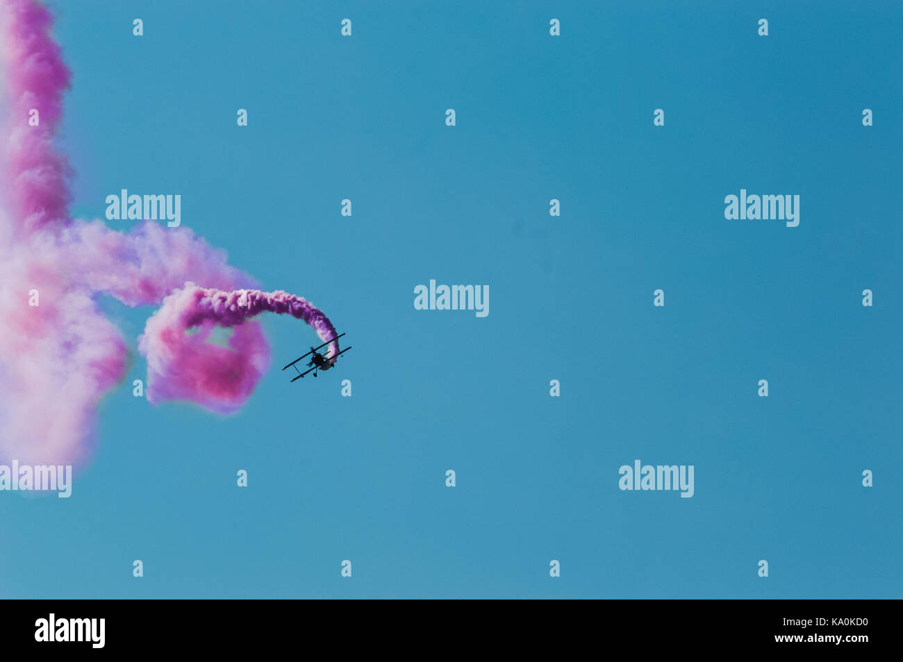 Aerobatic plane leaving a pink smoke trail in the bright blue sky Stock ...