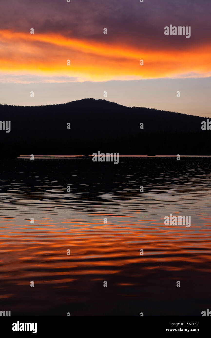 The waters of Butte Lake reflect the sunset with the silhoutte of ...