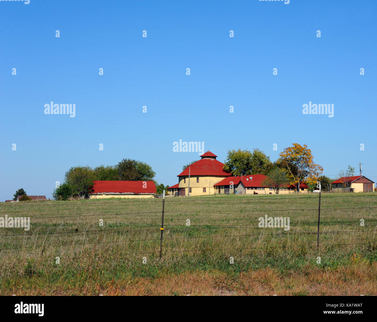 Round wooden barn has red shingled roof. Home and outbuildings are ...