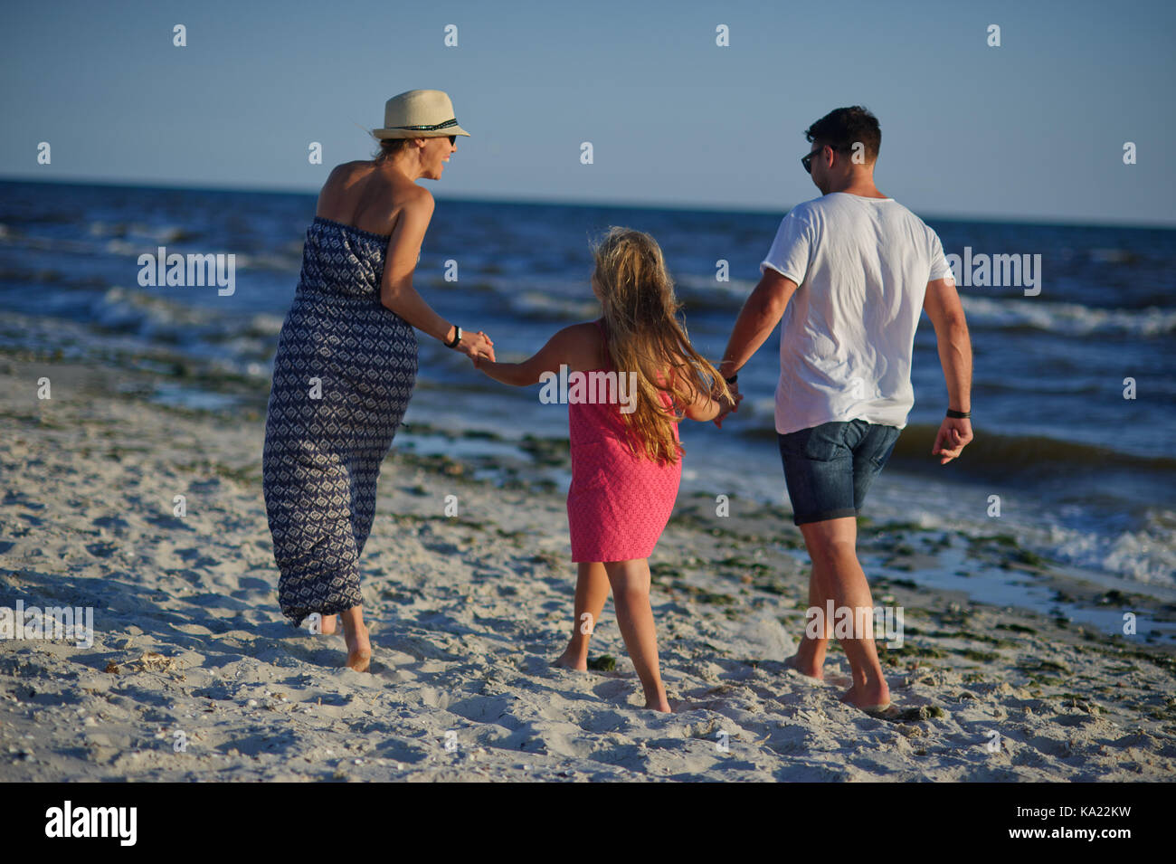 Happy family walks along the seaside holding hands. The blue sky, the ...