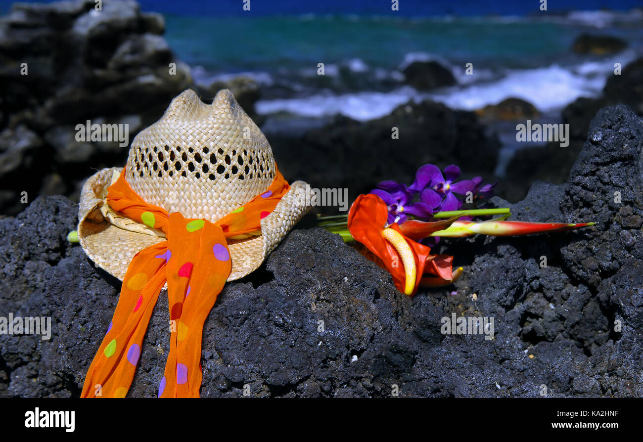 Straw hat, wrapped with a colorful orange scarf, lay across lava rocks ...