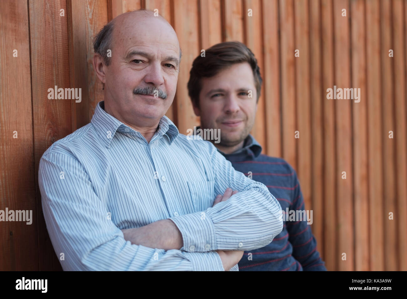 Father and son stand together near wooden background Stock Photo - Alamy
