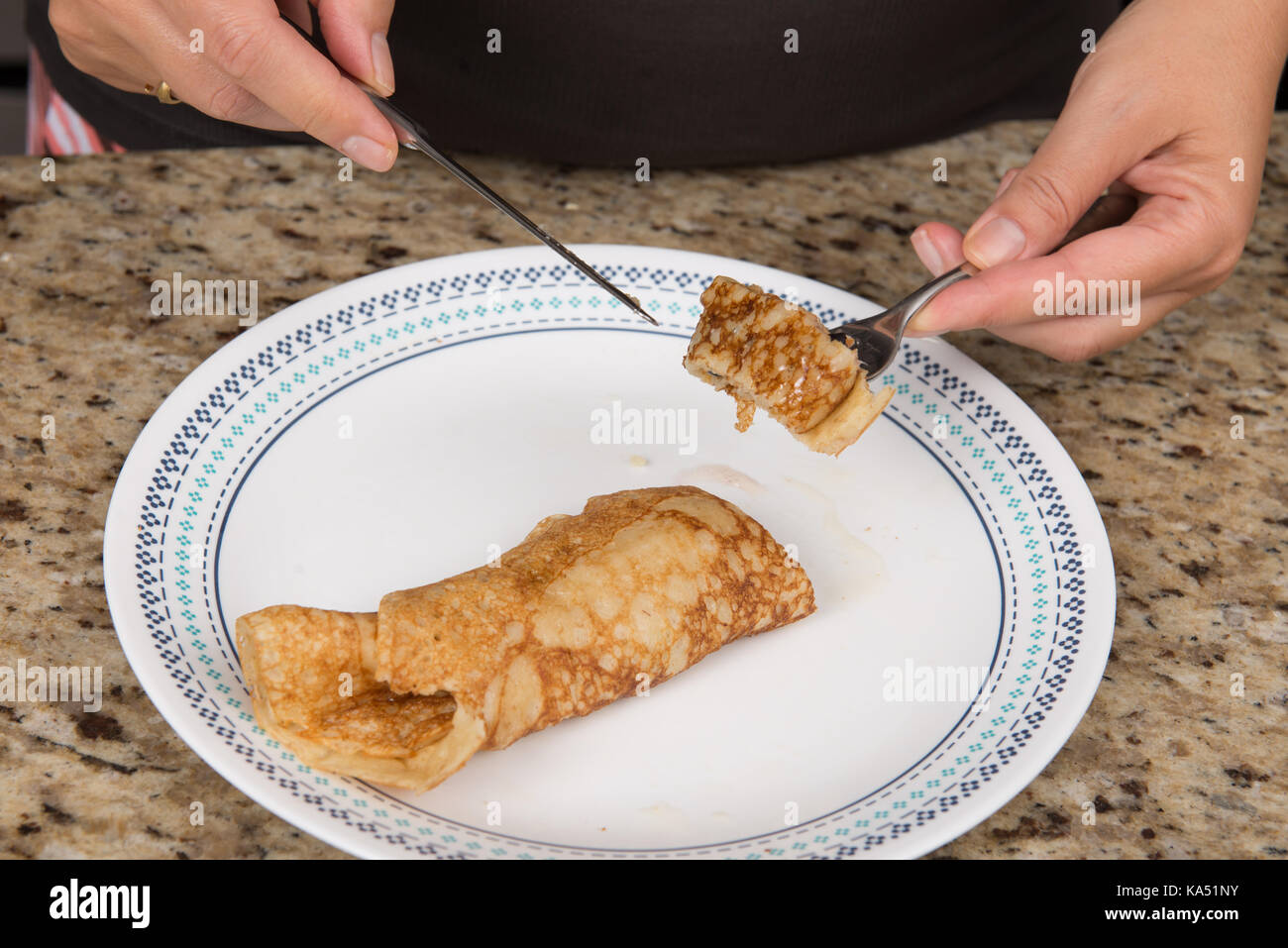 Close-up of woman's hands getting ready to eat crepes with knife and ...