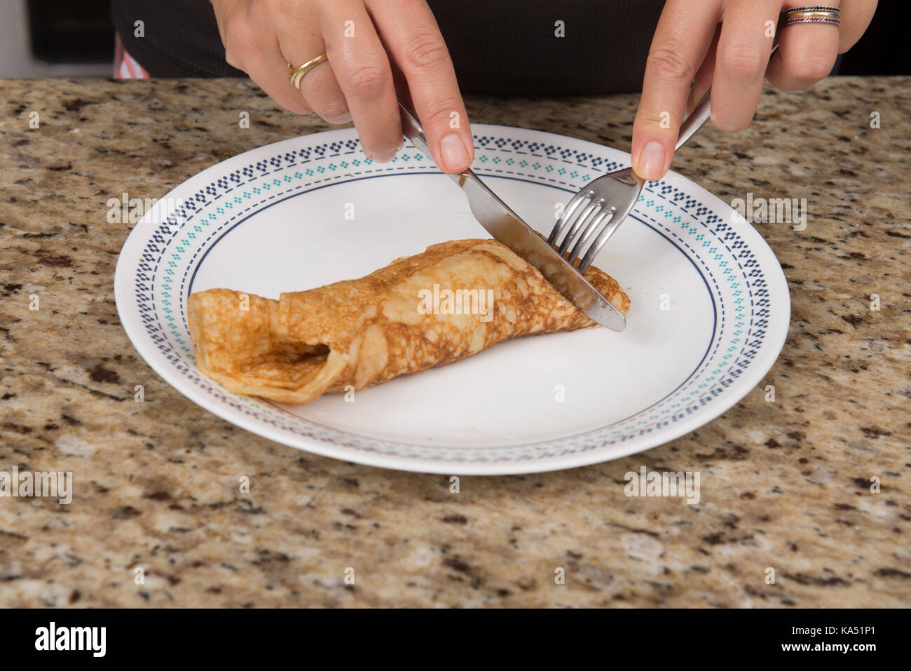 Close-up of woman's hands getting ready to eat crepes with knife and ...