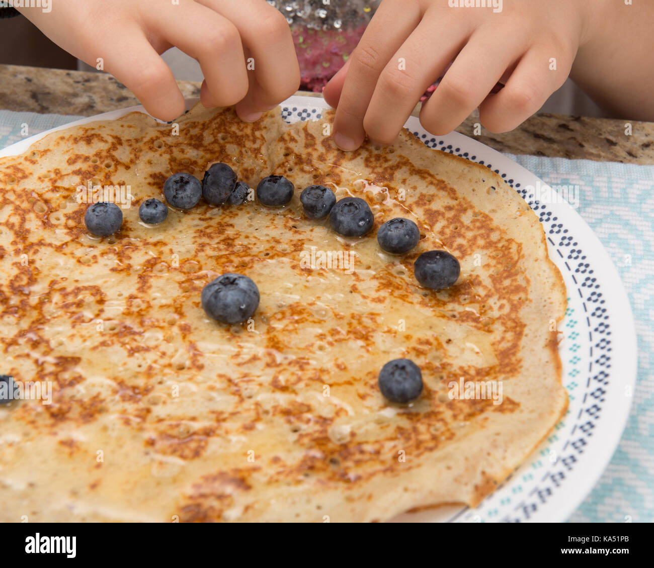 Close-up of child's hand preparing crepes with blueberries and honey ...