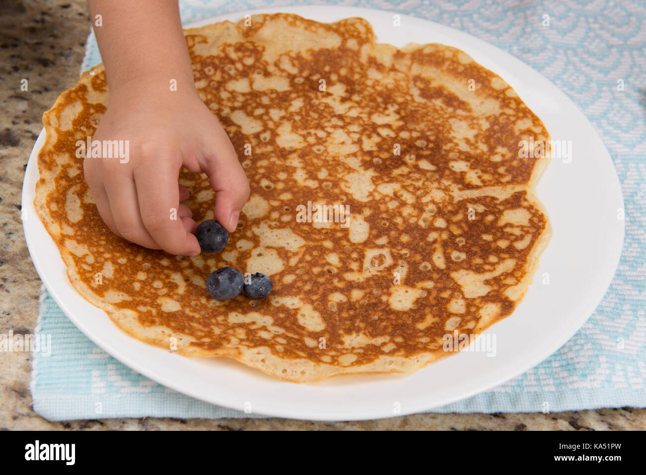 Close-up of child's hand preparing crepes with blueberries and honey ...
