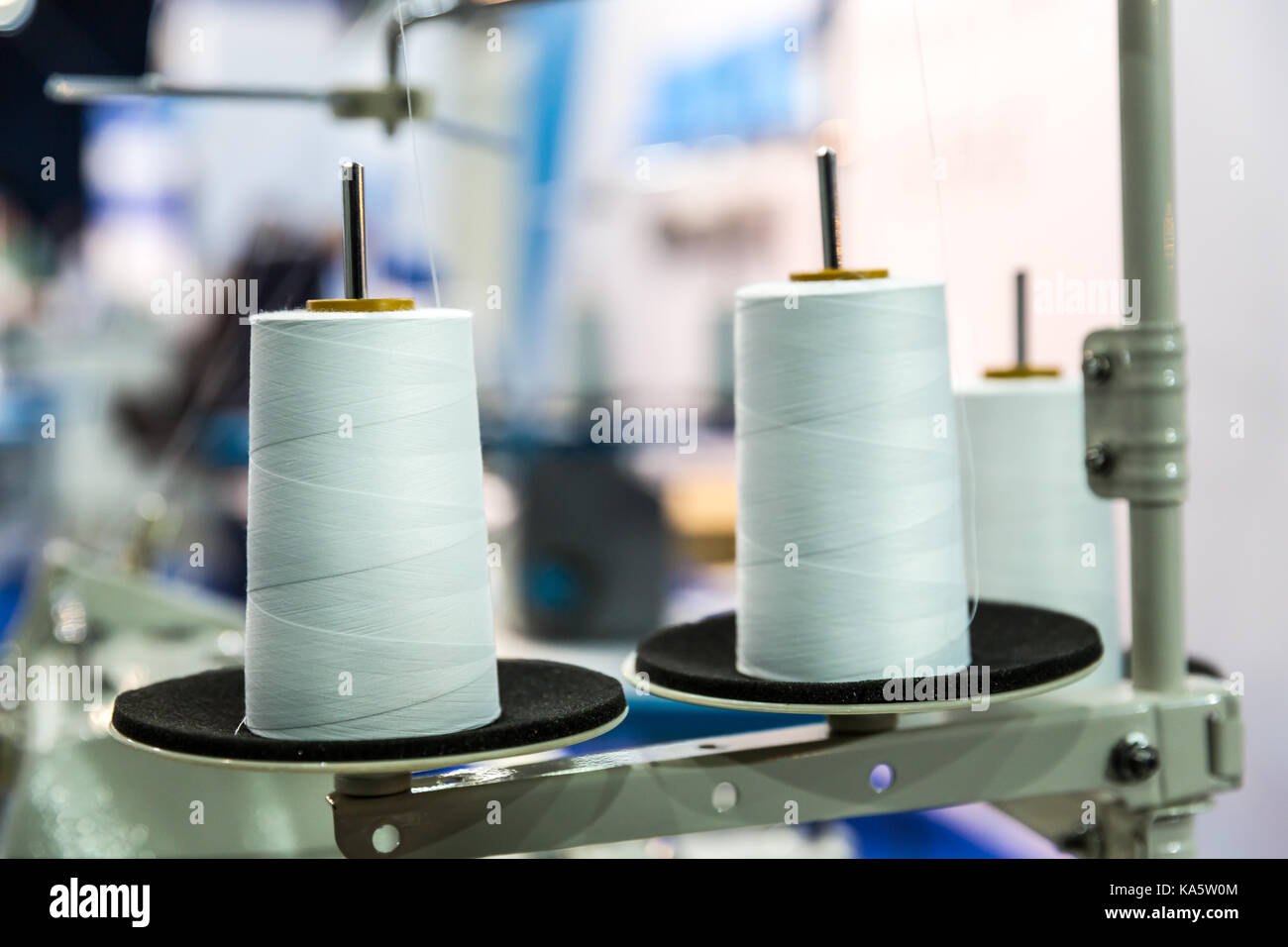 Spools of white threads on sewing machine, closeup. Cloth factory, weaving, textile production ...