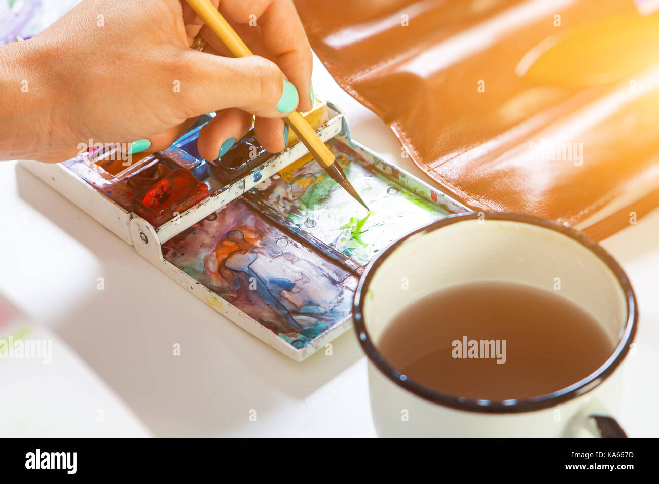 Close-up artist with bright nails dabs a brush in a pallet with a ...
