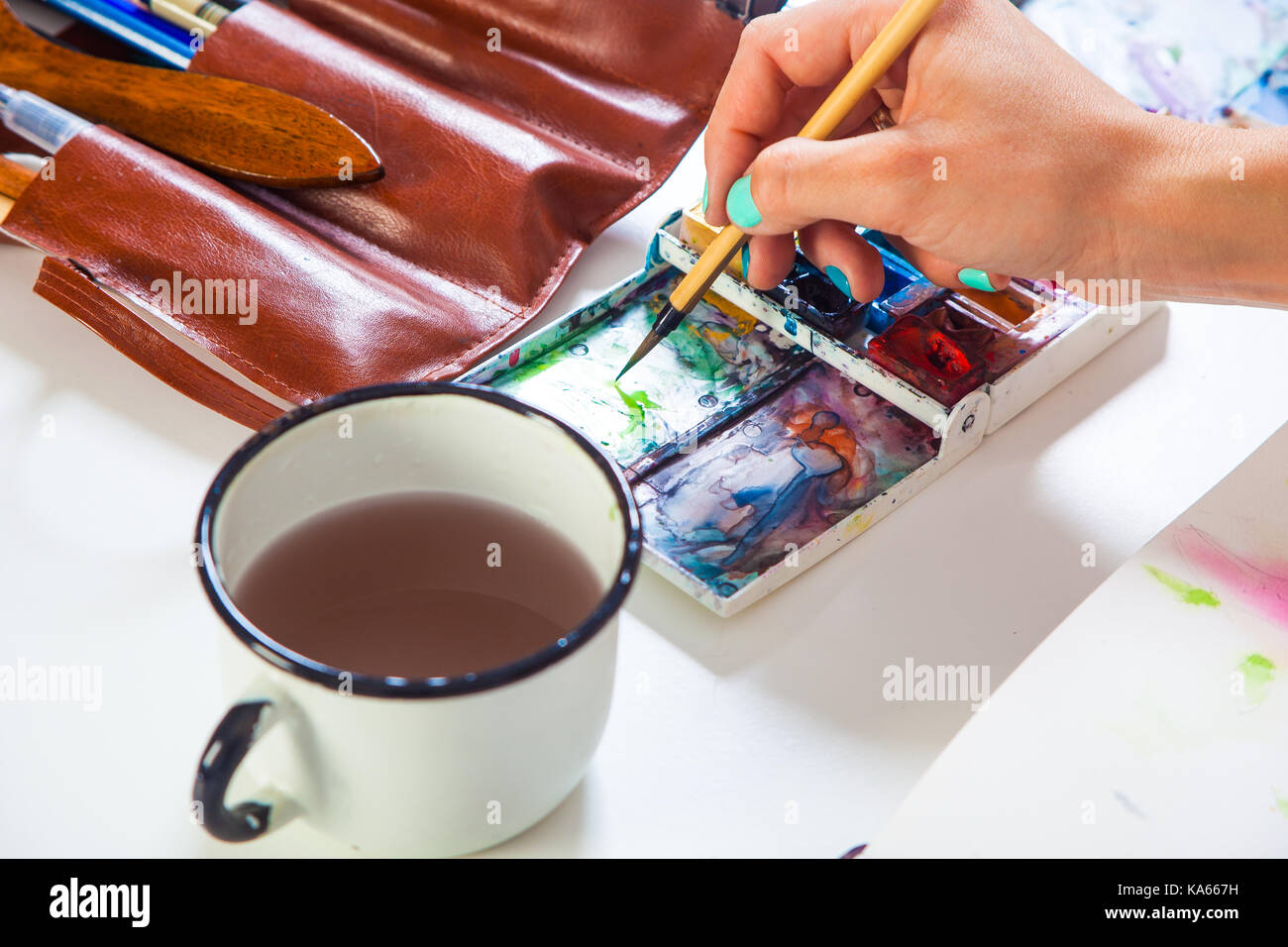 Close-up artist with bright nails dabs a brush in a pallet with a ...