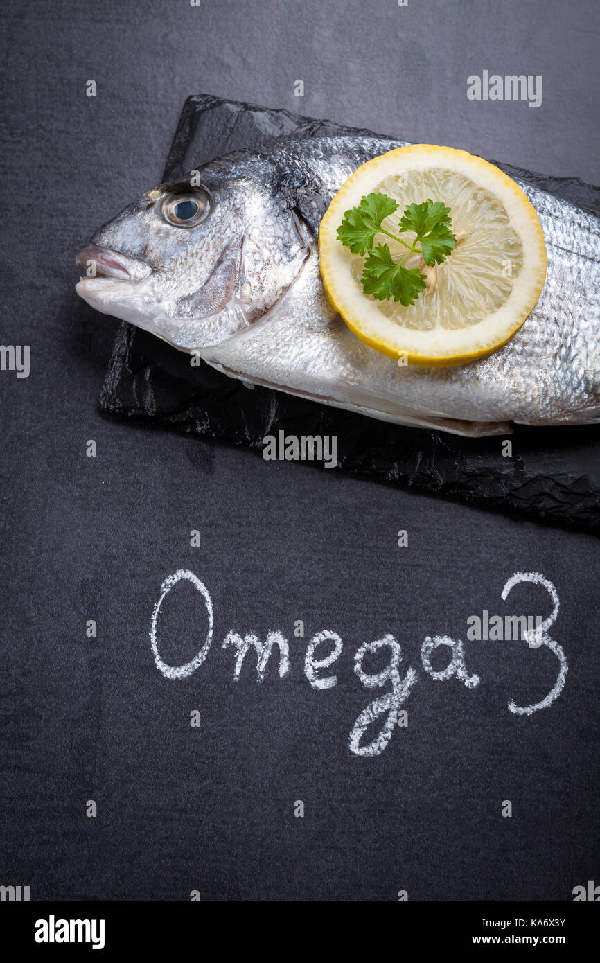 Raw dorada fish laying on black slate and written word omega 3 by white ...