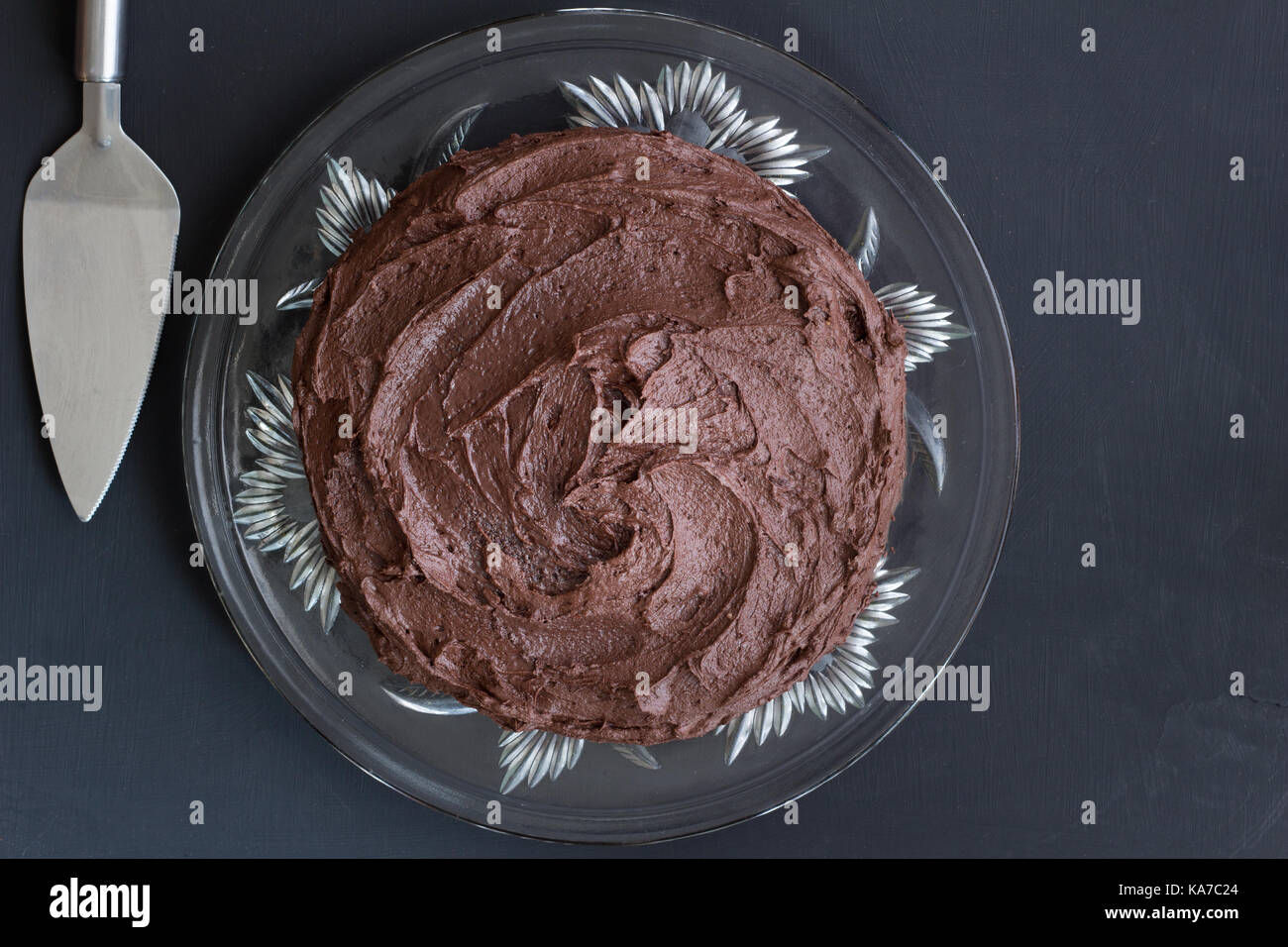 Top view of rich chocolate cake on glass plate with server on black ...