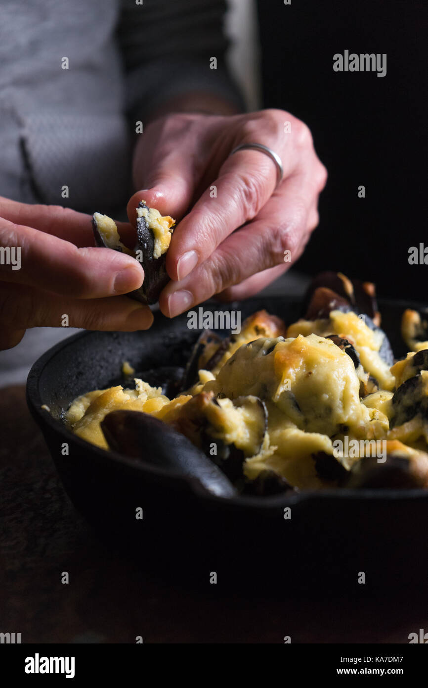 Female hands over a frying pan with mussels under cheese sauce vertical ...