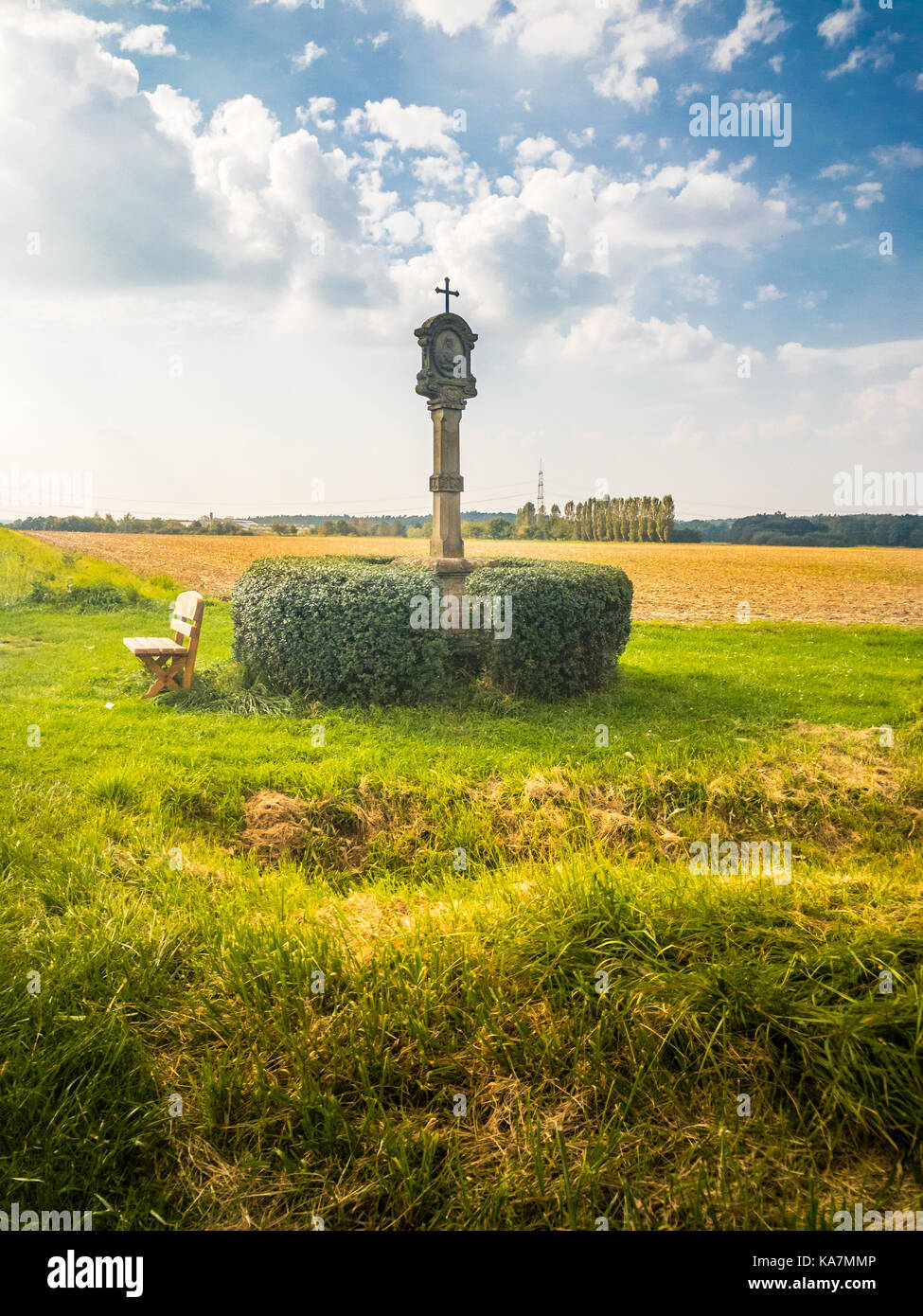 Classical piety column in German nature with a wooden bench in front of ...
