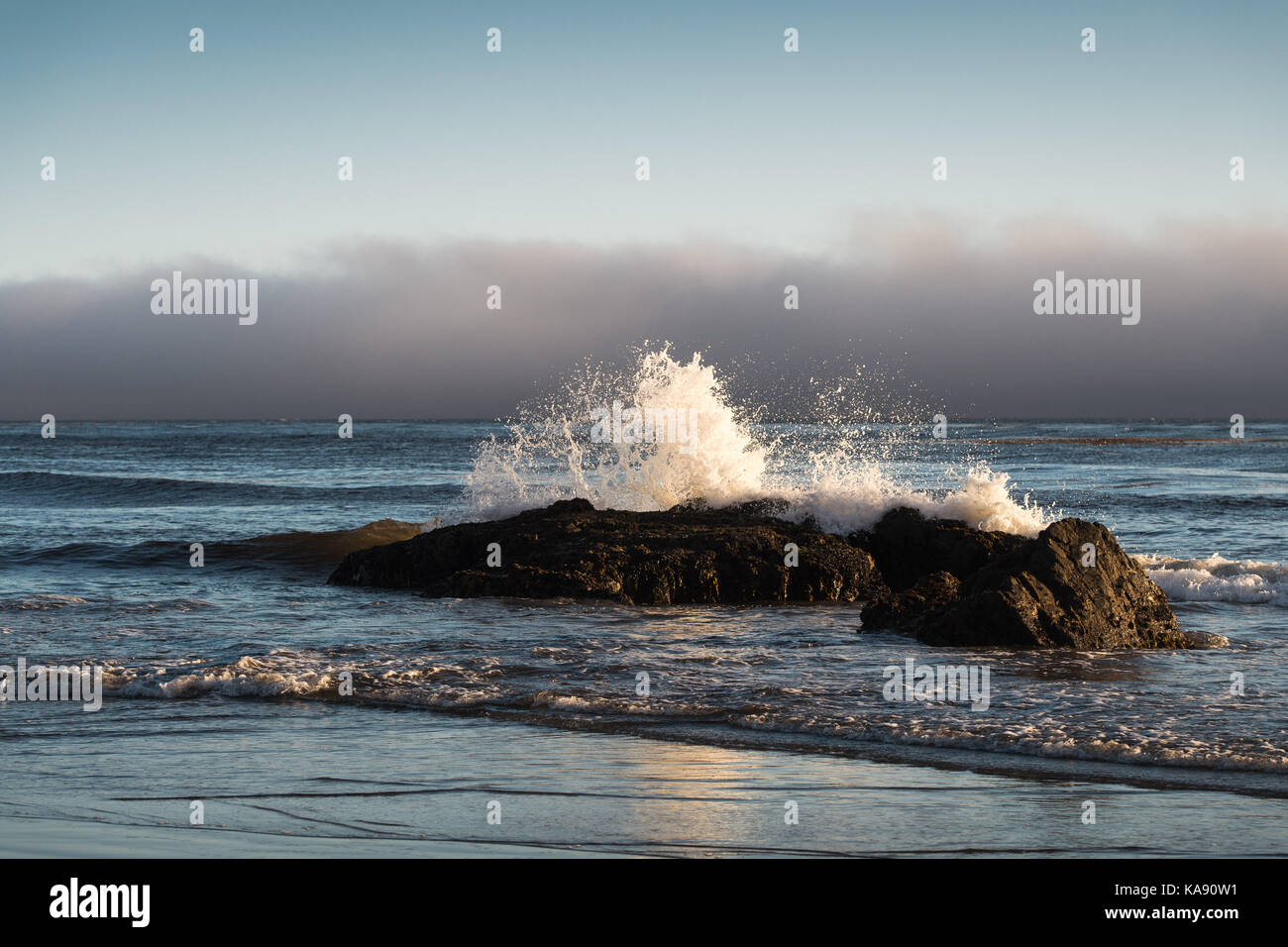 A wave hits a rock at sunset on the beach in San Simeon, California ...