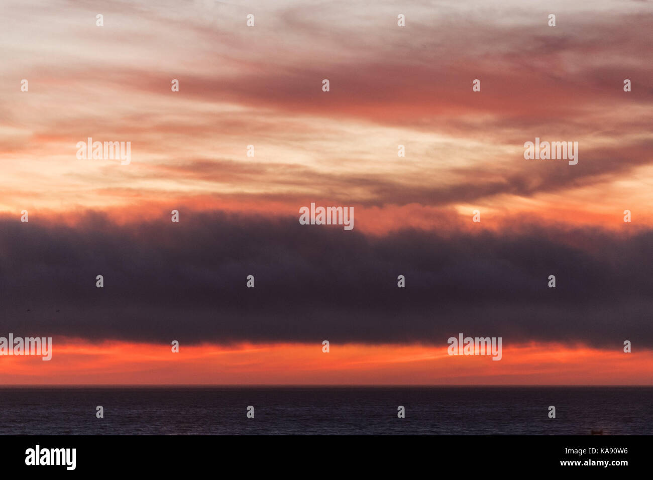 A dramatic red sunset with a thick band of dark cloud over the Pacific ...