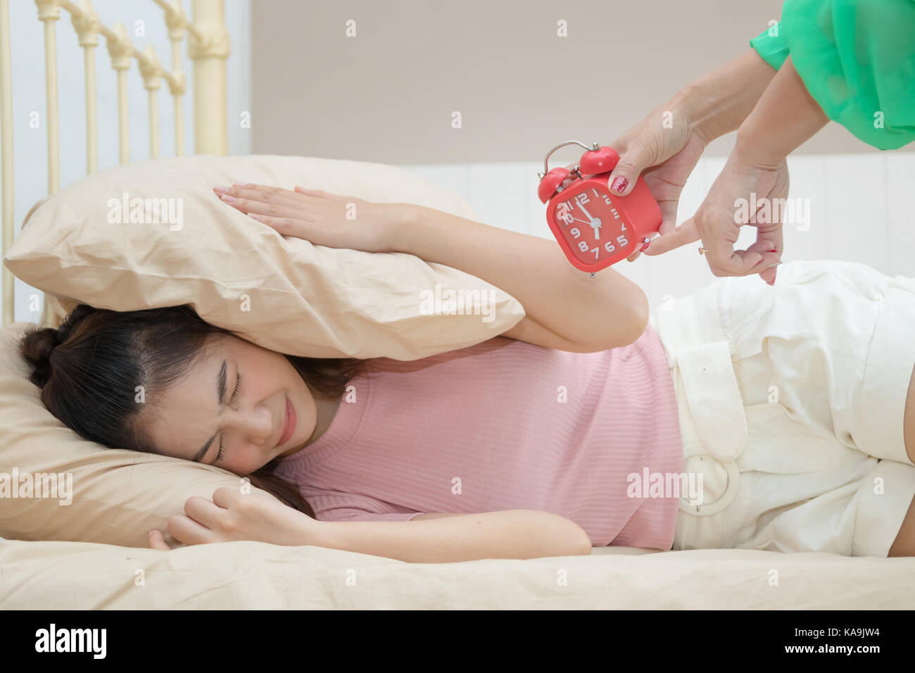Mother's holding an alarm clock and waking up her teenage daughter at ...