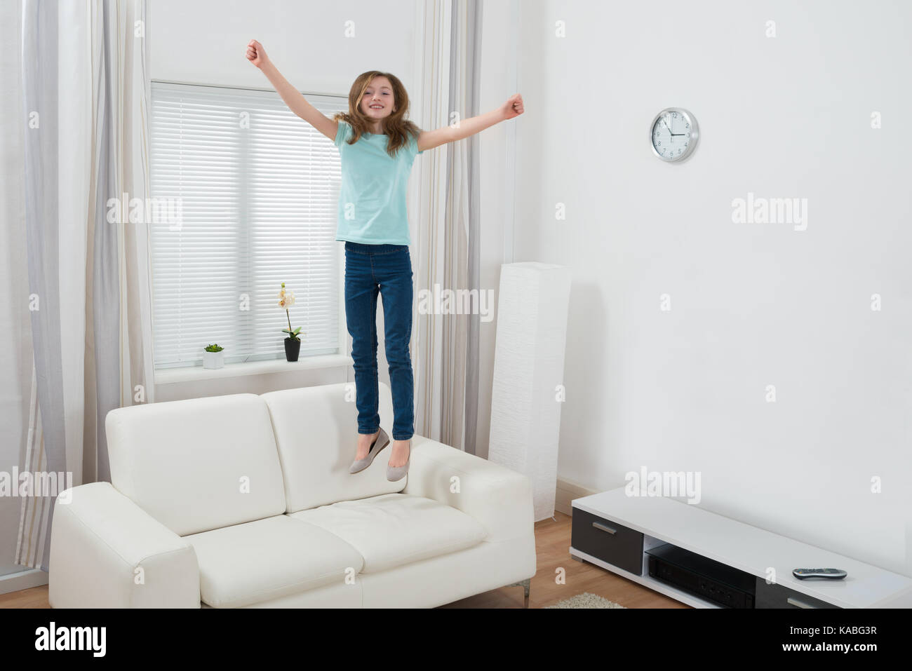 Excited Girl Jumping On White Sofa In Living Room At Home Stock Photo ...