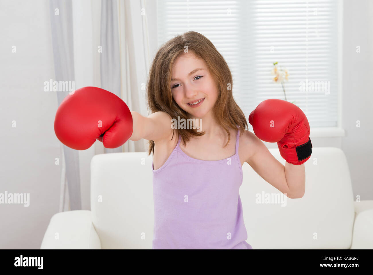 Cute Girl Punching With Boxing Gloves In Living Room Stock Photo - Alamy